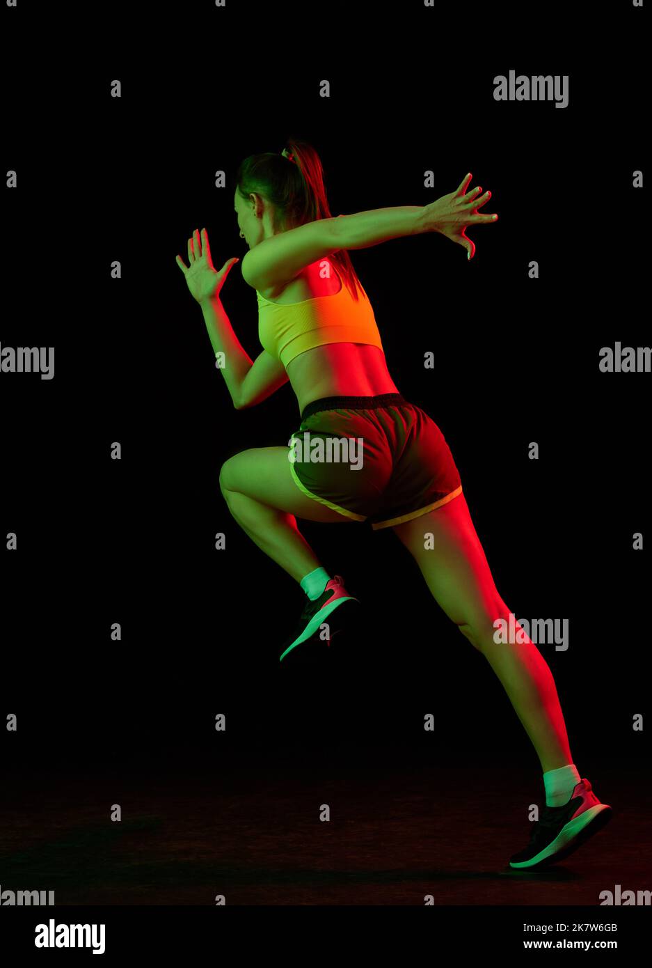 Professional female athlete running isolated on dark background in neon ...