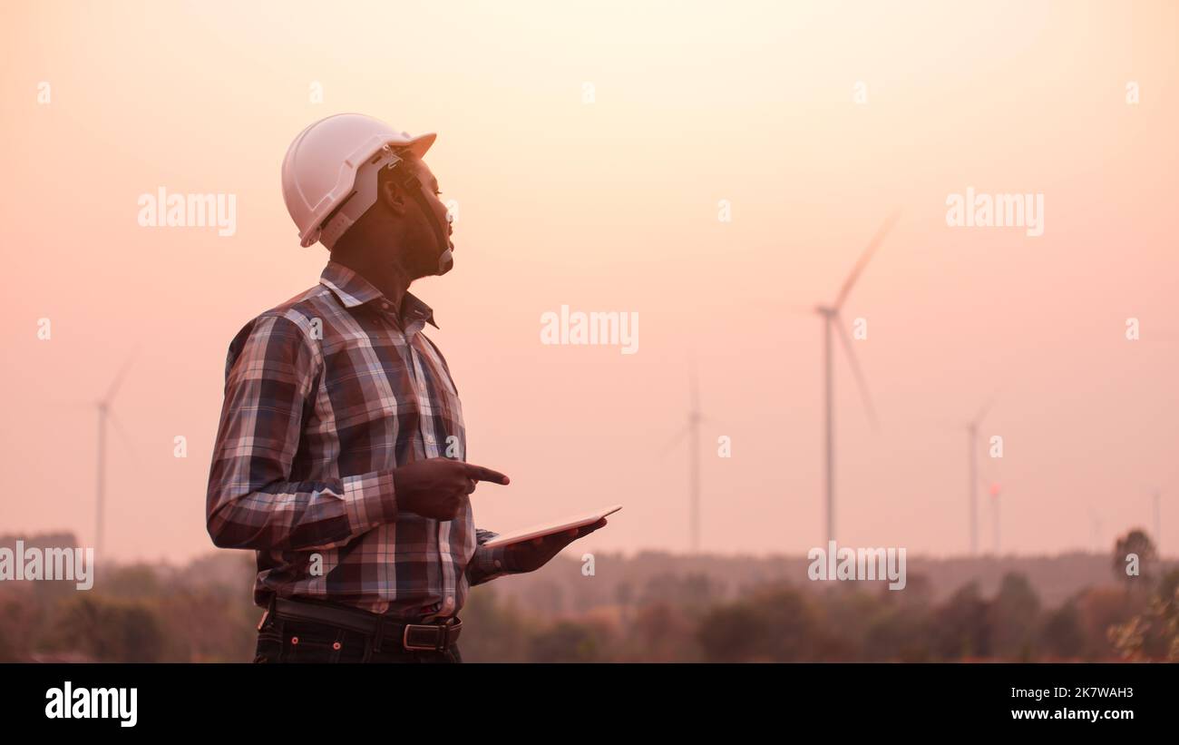 African engineer man stands holding tablet front the wind turbines ...