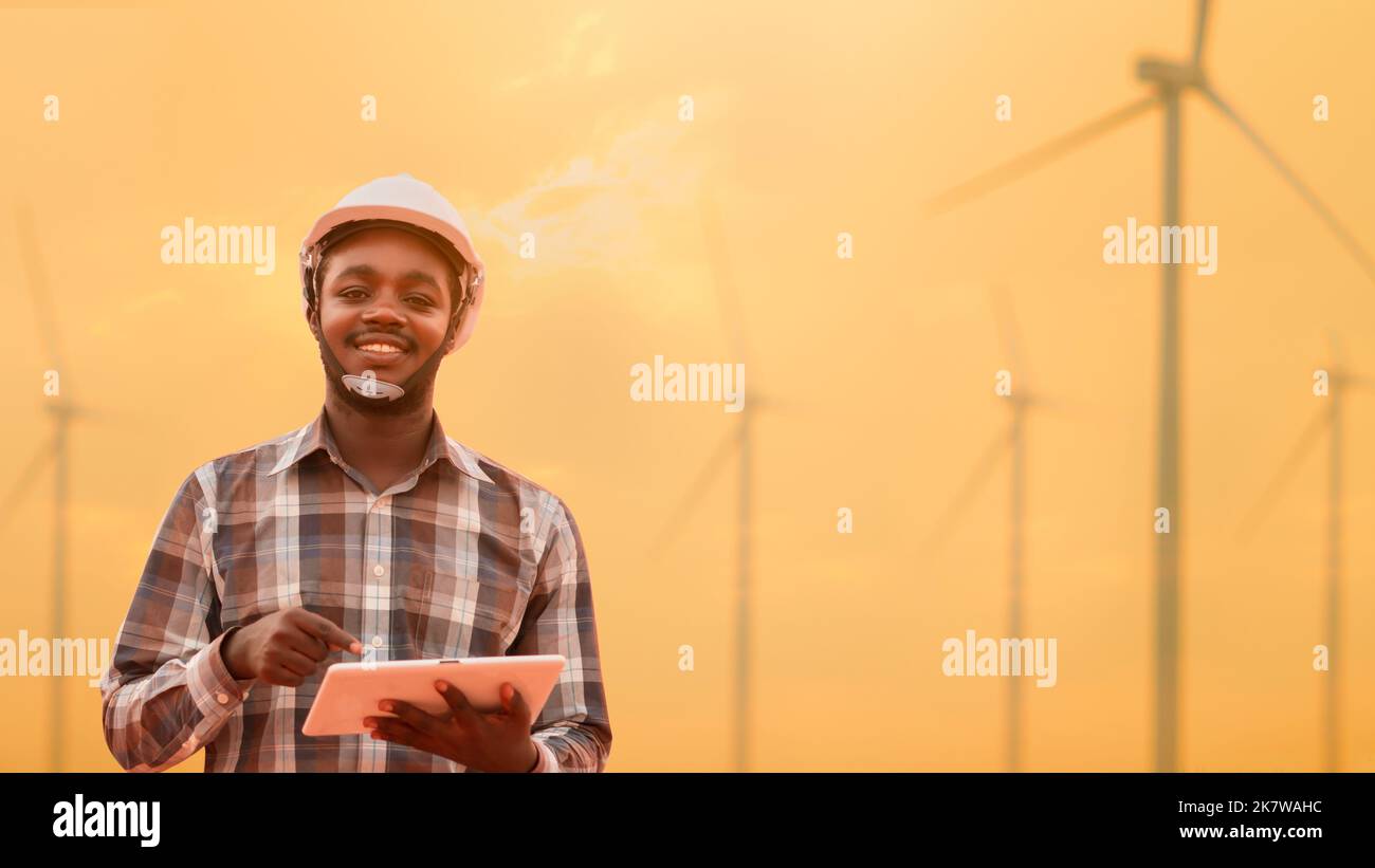 African engineer man stands holding tablet front the wind turbines ...
