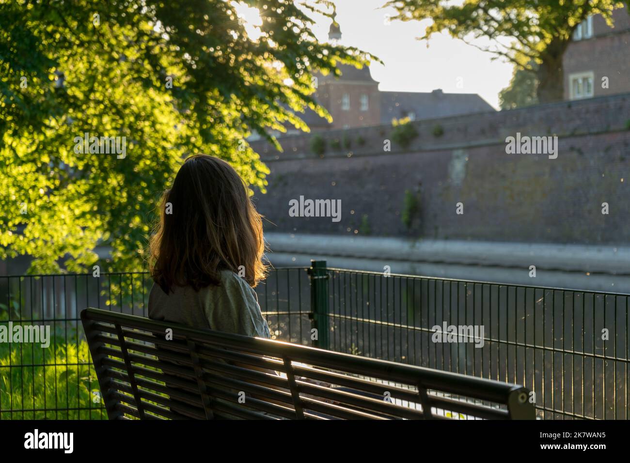 Woman sitting on a garden bench at sunset overlooking lake and historic ...