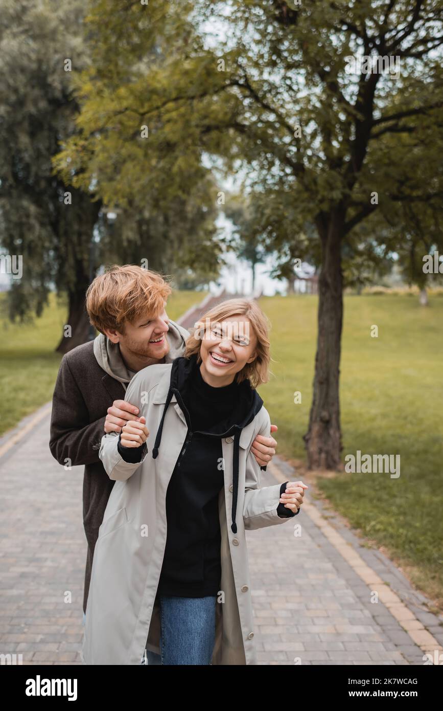 happy man hugging joyful young woman with closed eyes laughing in park ...