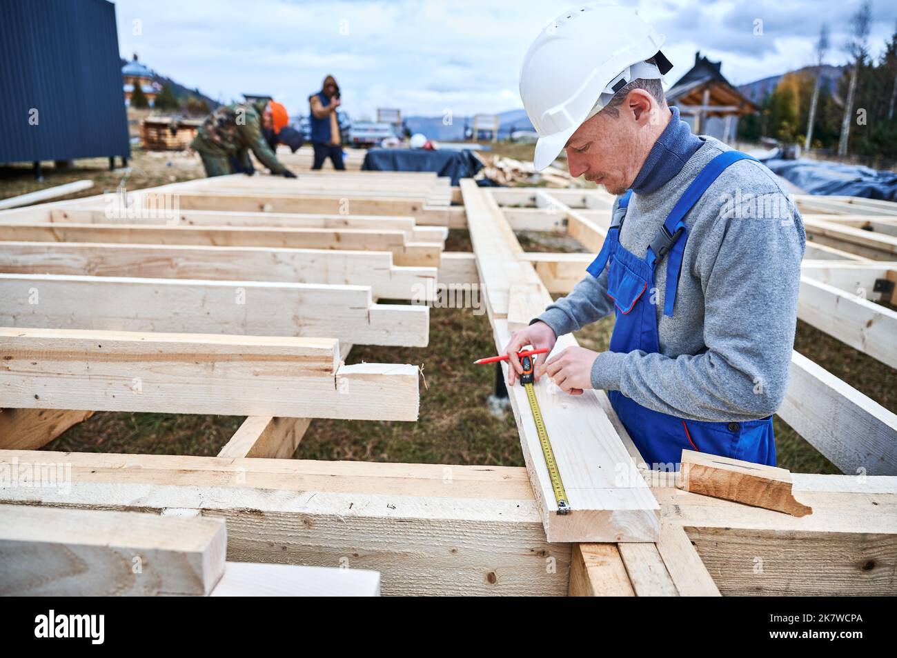 Man worker building wooden frame house on pile foundation. Carpenter using tape measure for ...