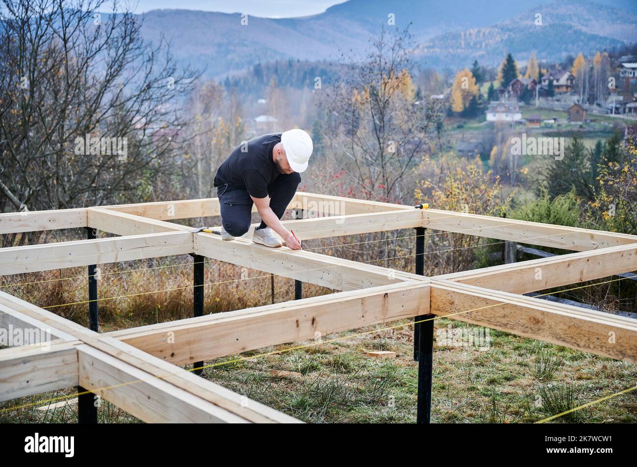 Man worker building wooden frame house on pile foundation. Carpenter ...