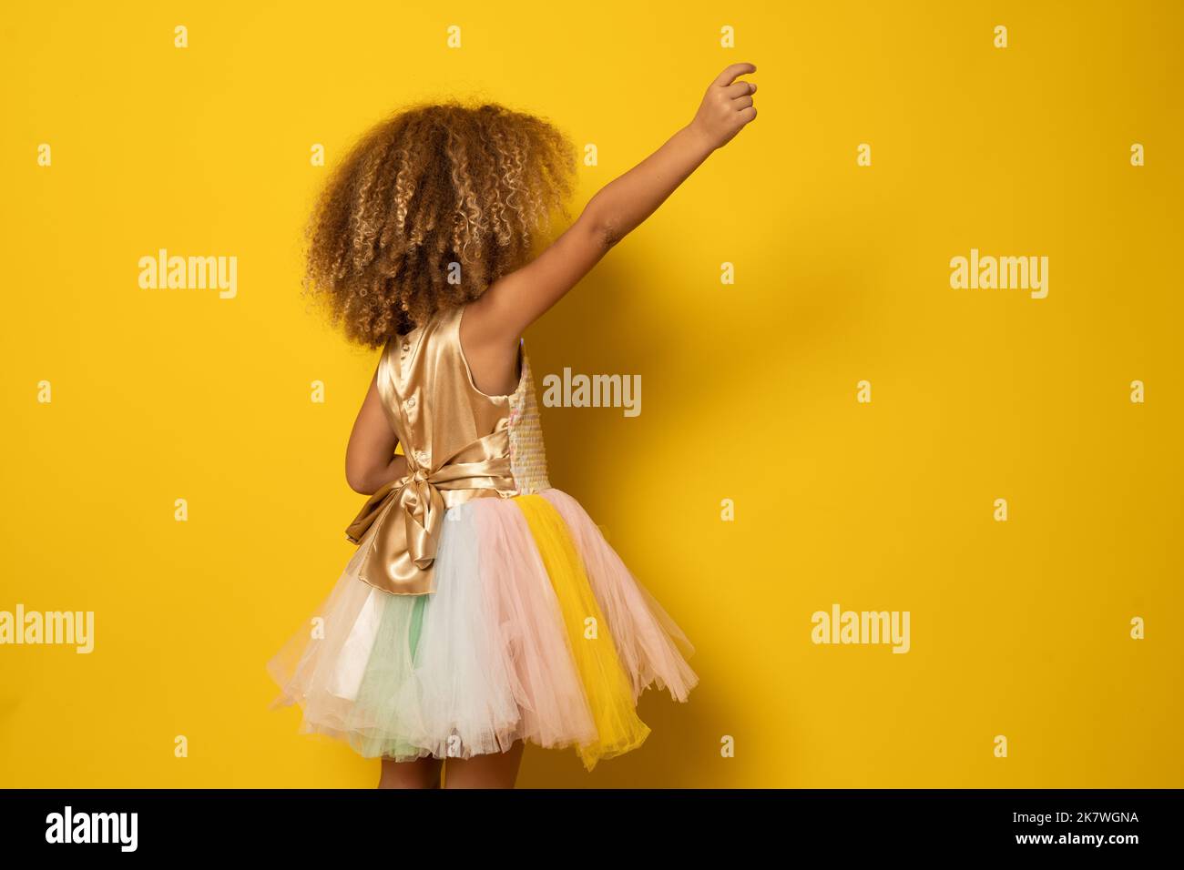 Back view of cute Little child dancing girl with curly hair pointing ...