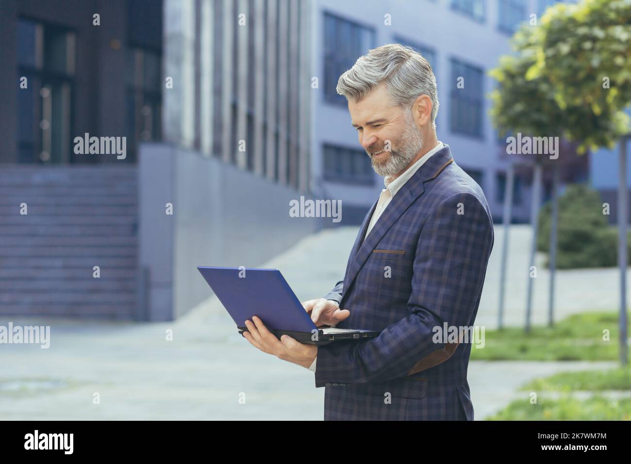 Happy and smiling boss using laptop while standing outside modern ...