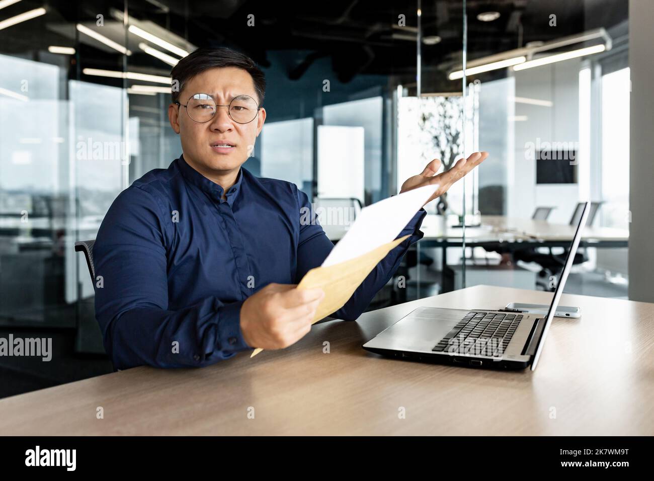 Annoyed asian businessman looking at camera and showing received letter ...