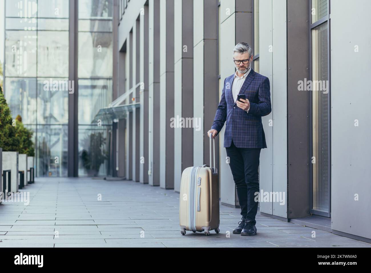 Business trip, senior gray-haired businessman outside hotel using phone ...