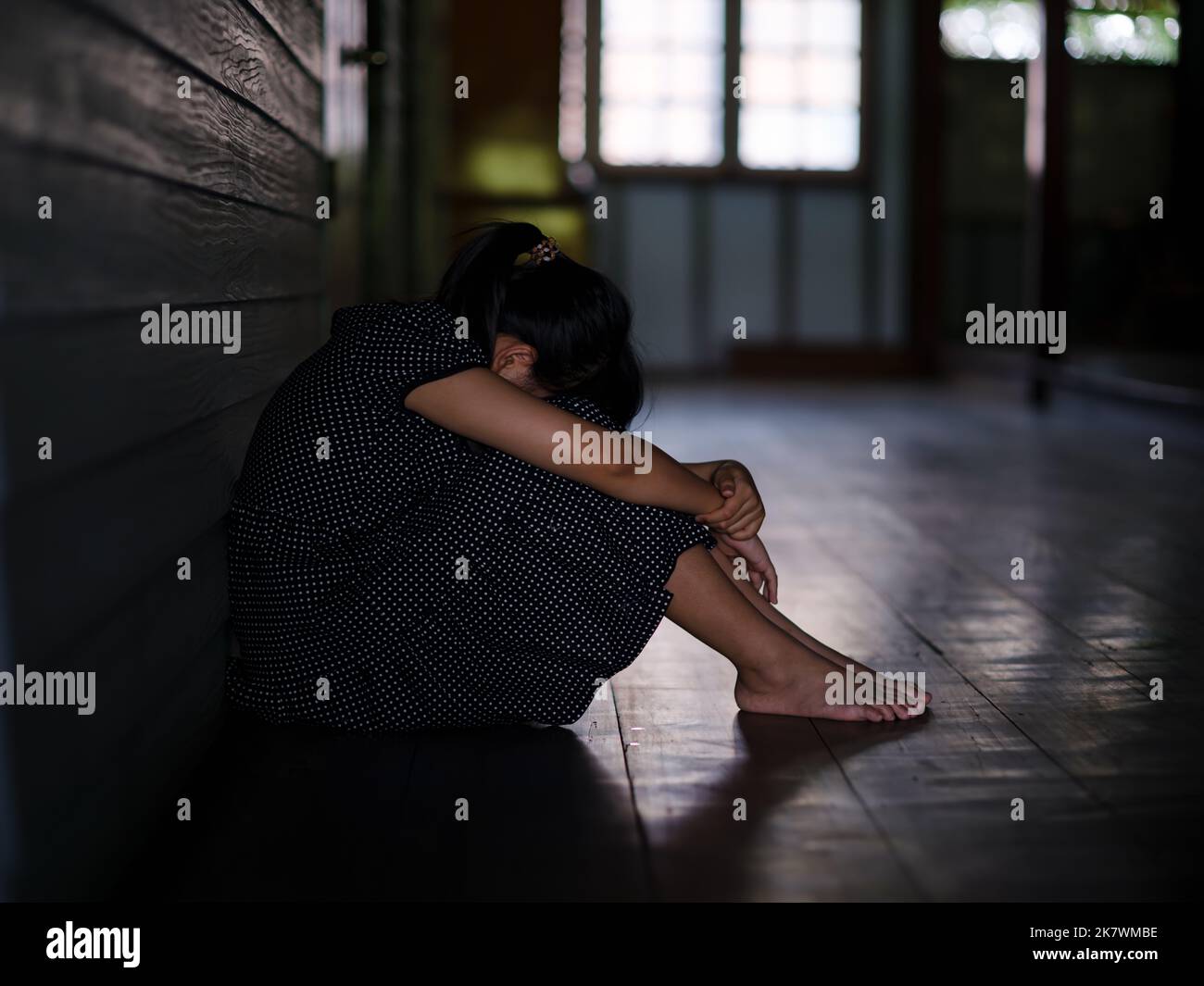 Sad lonely little girl crying while sitting on the floor in dark room ...