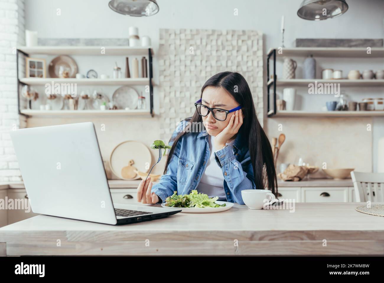 Lunch while working online. A young Asian woman sits in the kitchen at ...