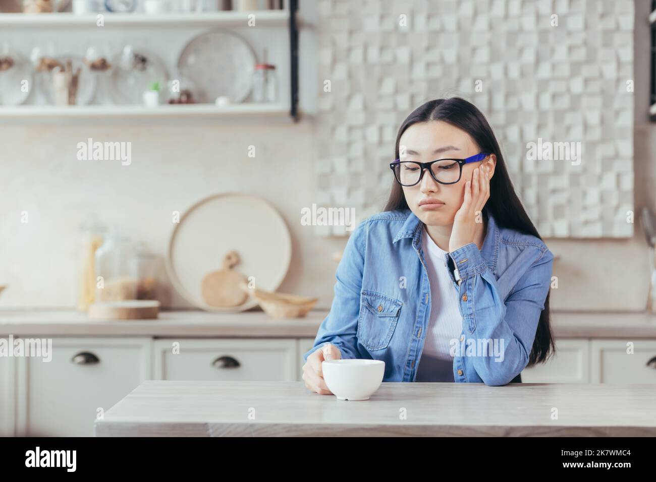 Coffee break. Young tired asian woman freelancer. Sitting at home at ...