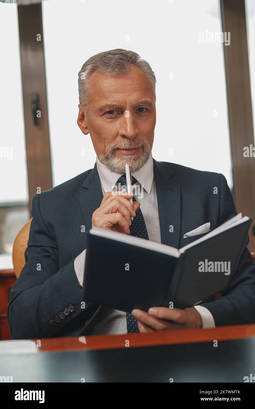 Focused Male hotelier making notes in diary while sitting in his office ...