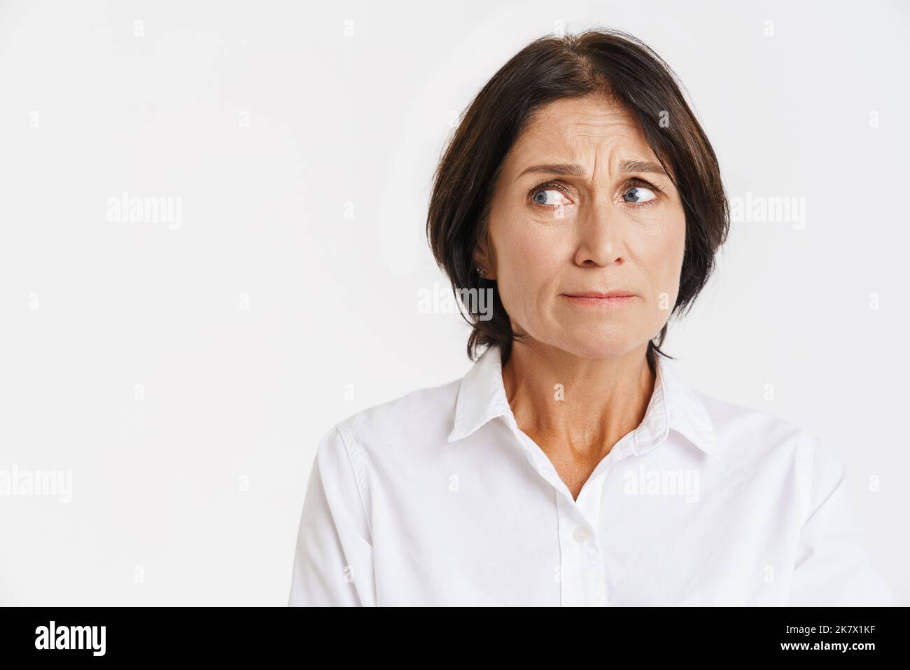 Mature brunette woman frowning and looking aside isolated over white ...