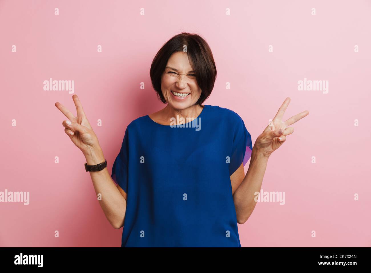 Mature woman making peace gesture while laughing at camera isolated ...
