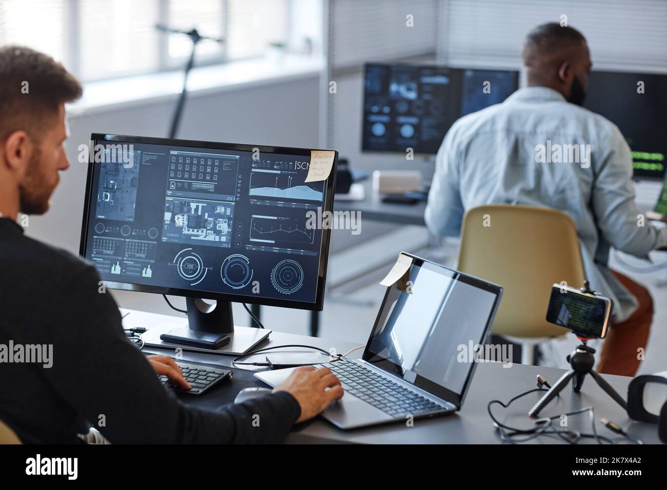 Portrait of male programmer or data specialist using computer in office with charts on screen ...
