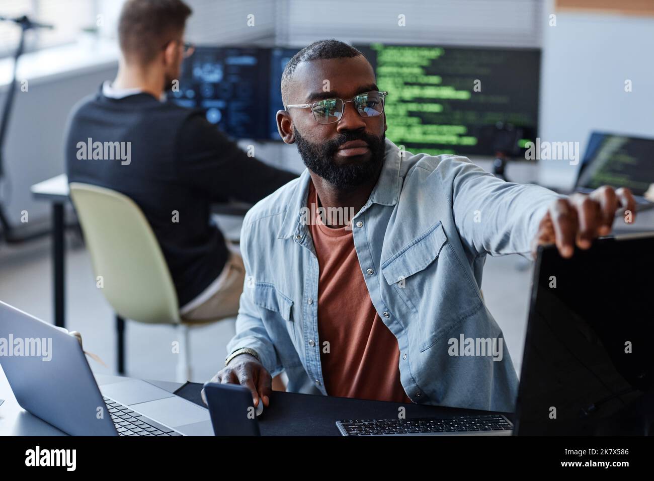 Portrait of black man adjusting computer screens while writing software code in office Stock ...