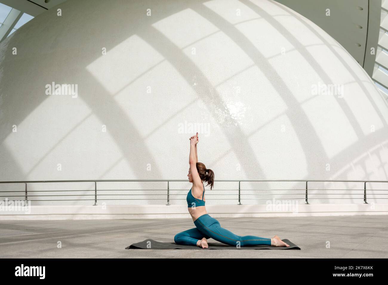 Sporty woman doing a pigeon yoga pose on a mat in a futuristic modern ...