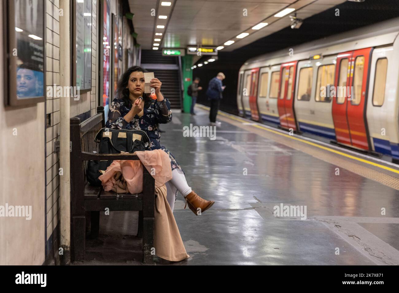 Woman putting on her make-up whilst sat on a London Underground station ...