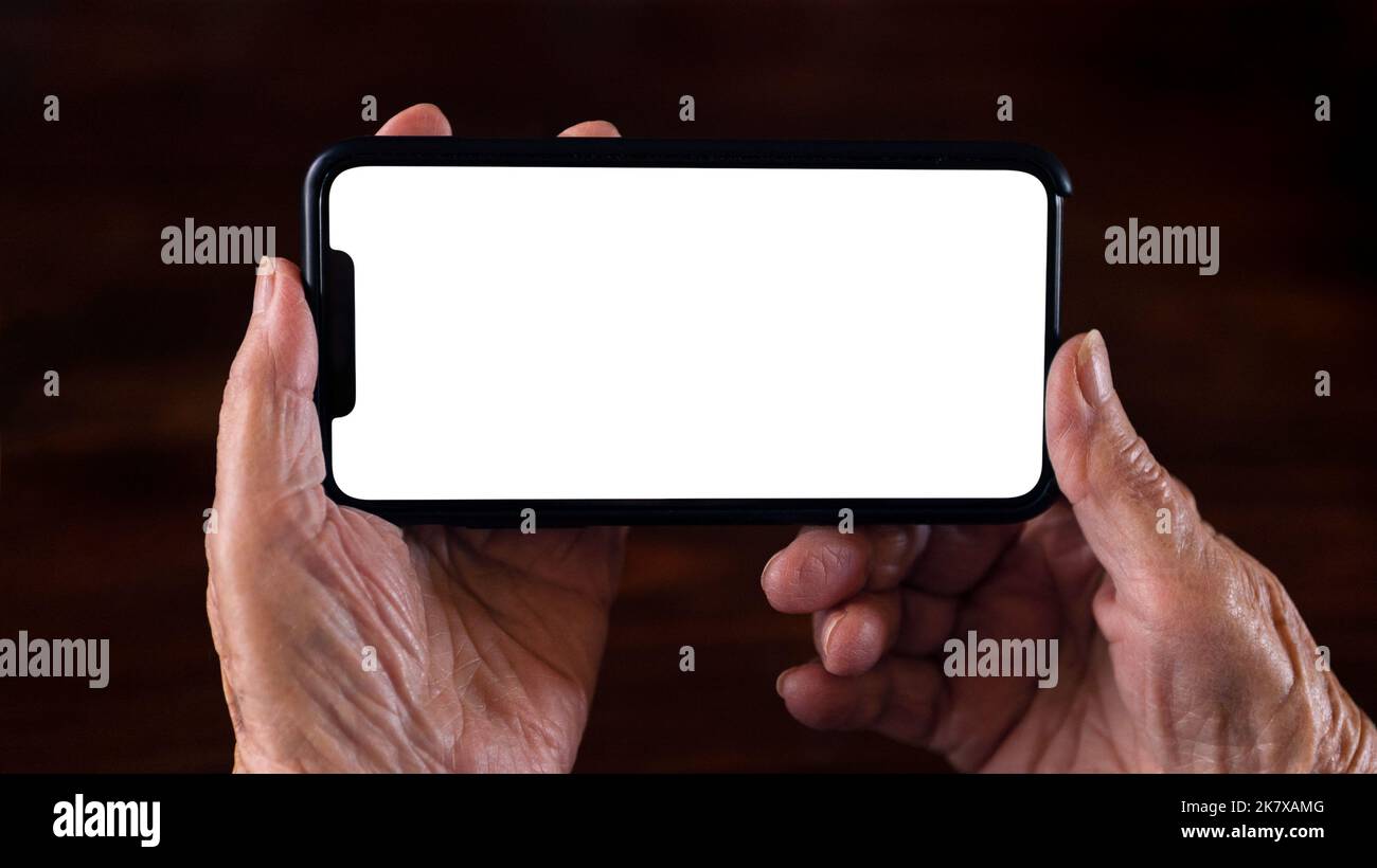 Wrinkled hands of the old woman holds a smartphone with white empty ...