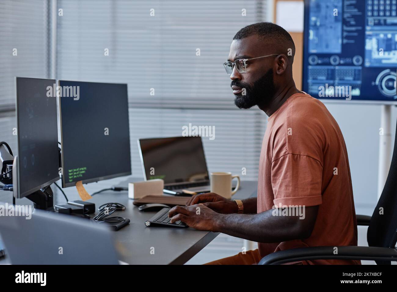 Side view of black software engineer using computer in high technology office, data systems and ...