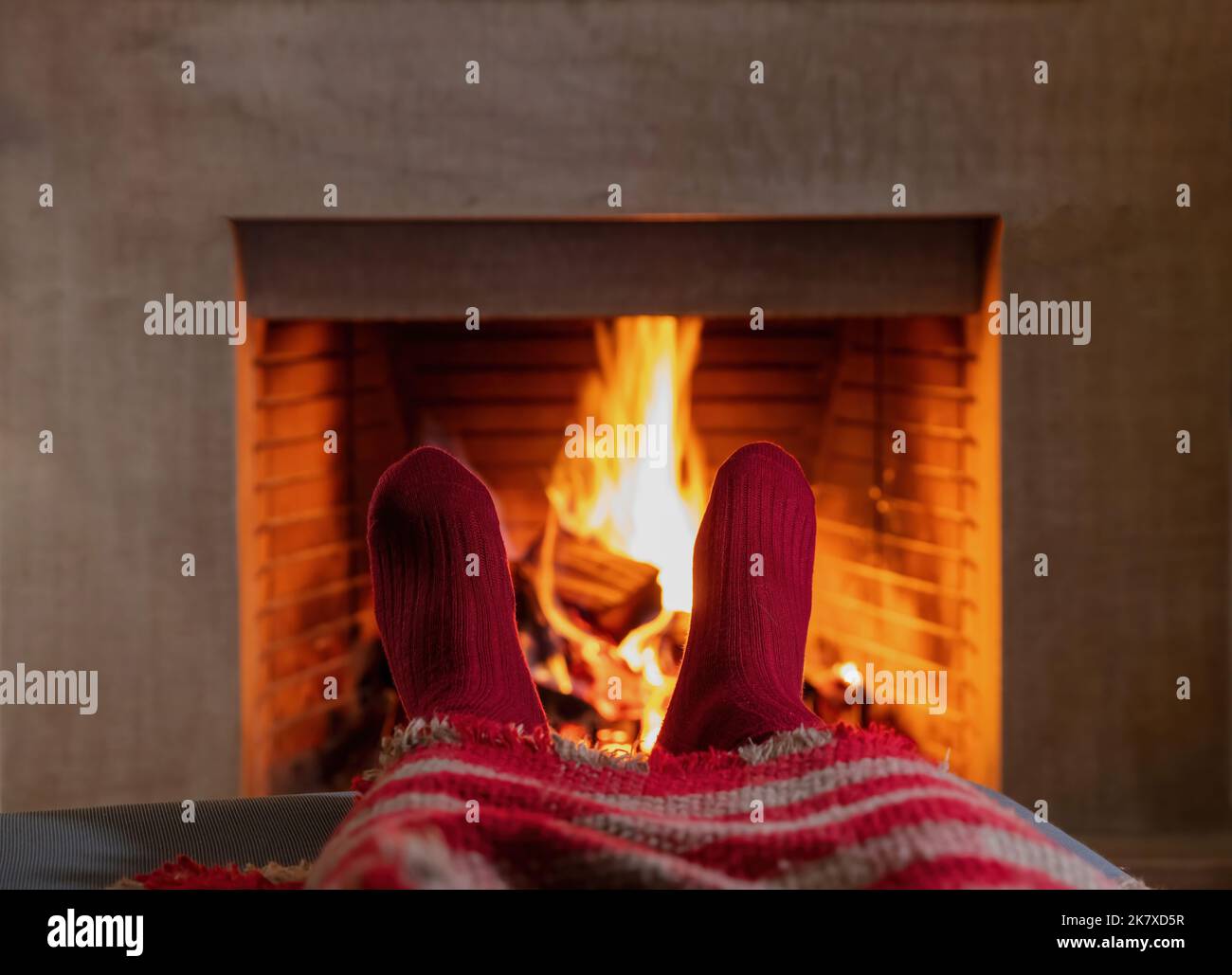 Man relaxing at the burning fireplace. Warm socks and blanket, fireside ...