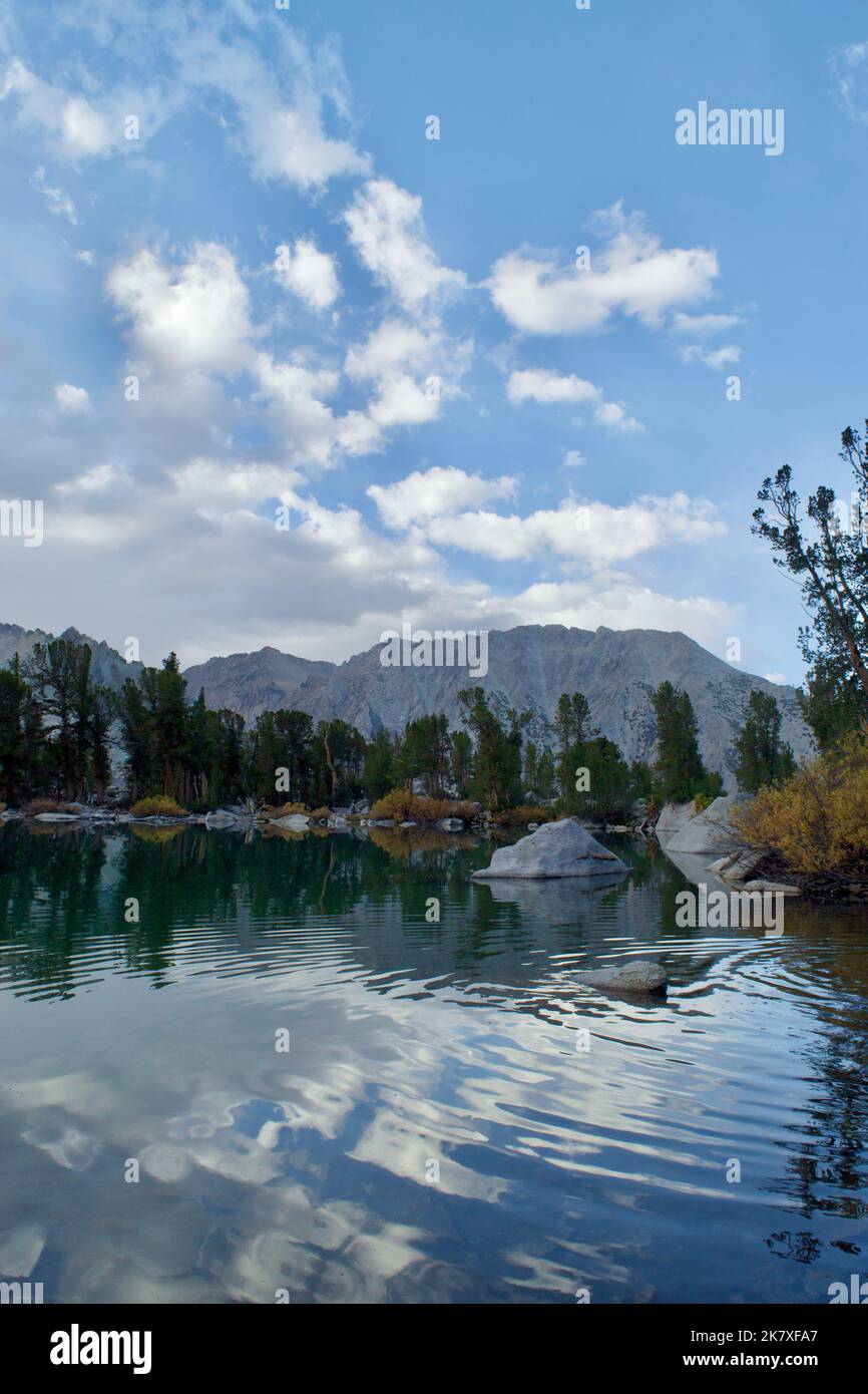 A vertical shot of a blue cloud sky reflected in an alpine lake with ...