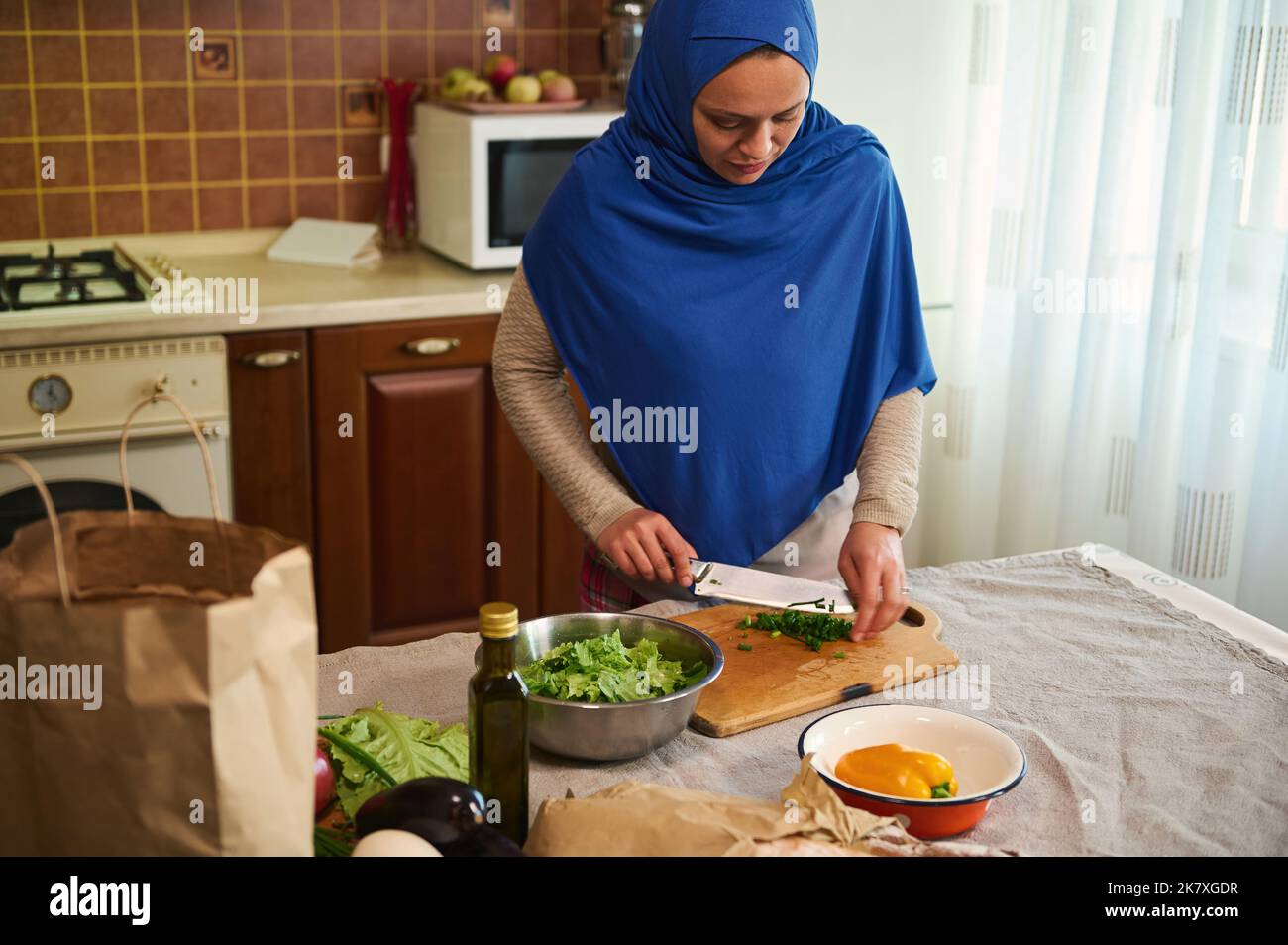 Pleasant Middle-Eastern Muslim woman housewife in hijab chopping greens ...