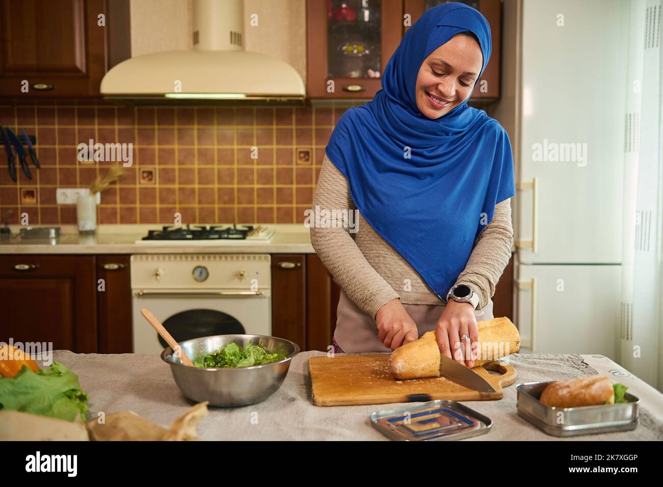Pleasant Middle-Eastern Muslim woman housewife in a blue hijab cutting ...