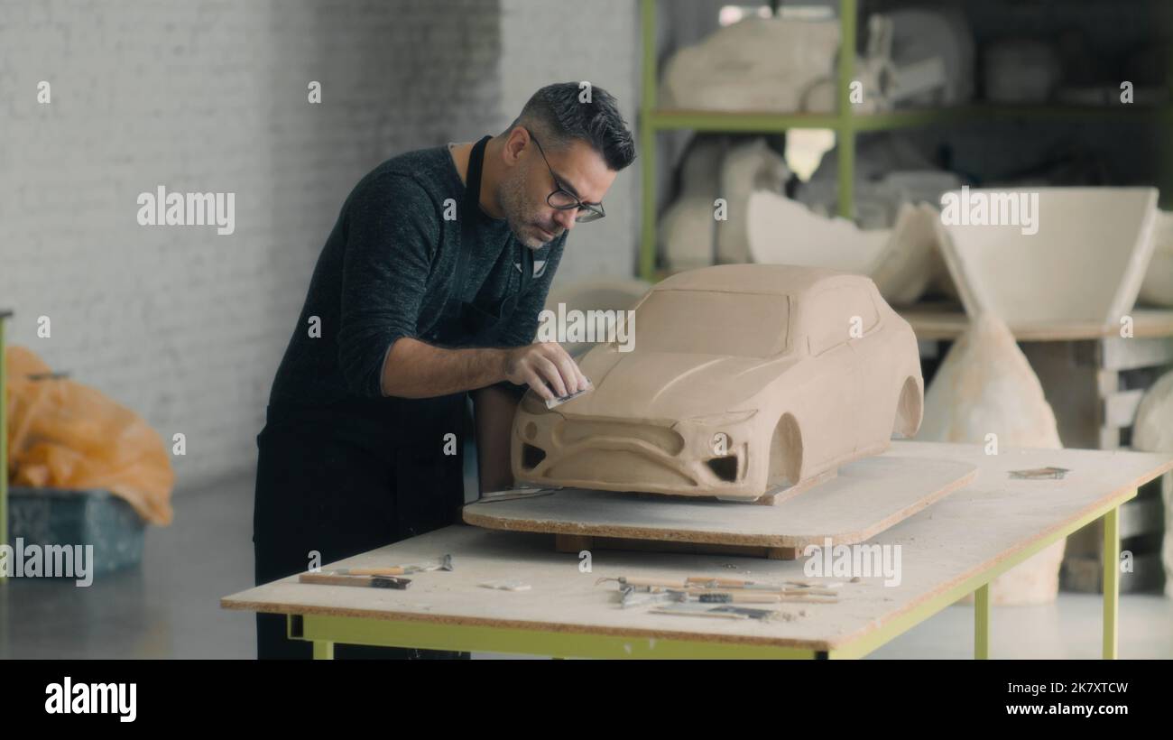 Experienced car designer with an apron works on the sculpture of the ...