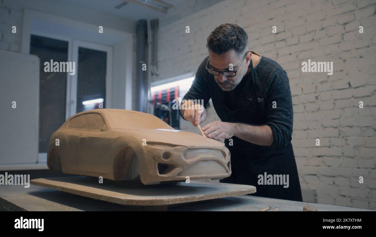 Experienced designer works on the sculpture of the car made of raw clay ...