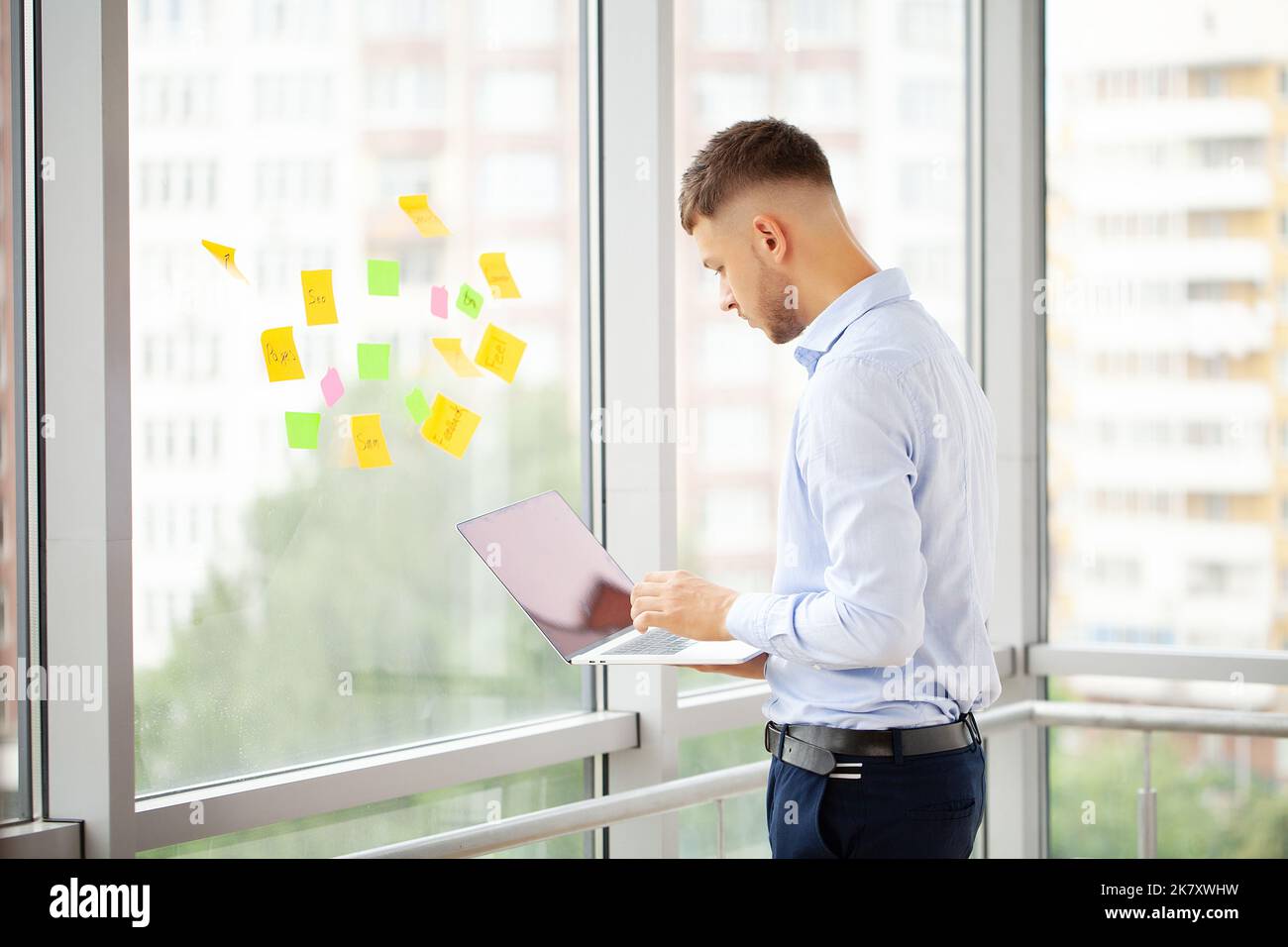 Portrait of handsome young man holding laptop standing by window Stock ...