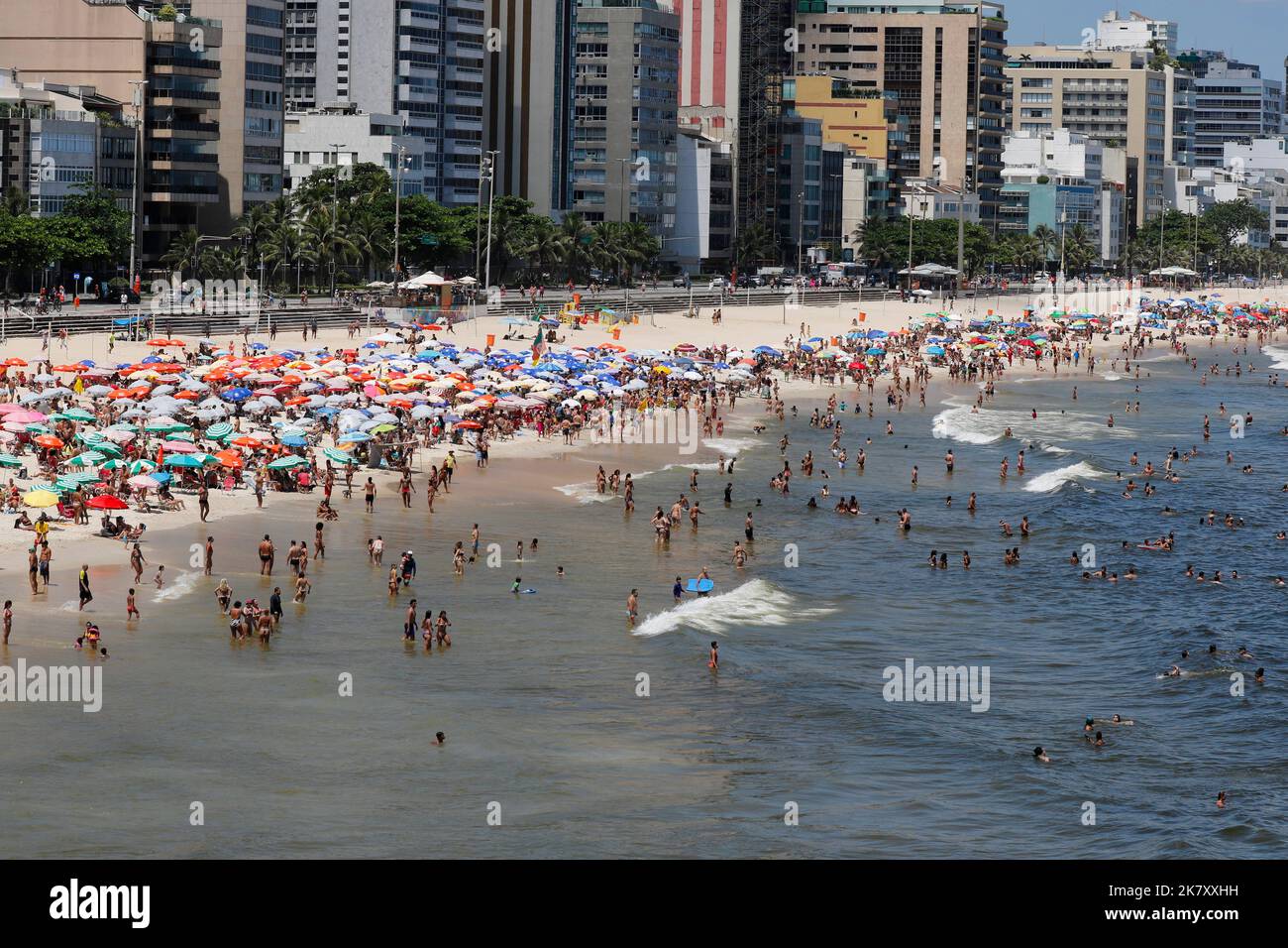 Leblon beach, Rio de Janeiro, Brazil. People sunbathing near shore with colorful umbrellas ...