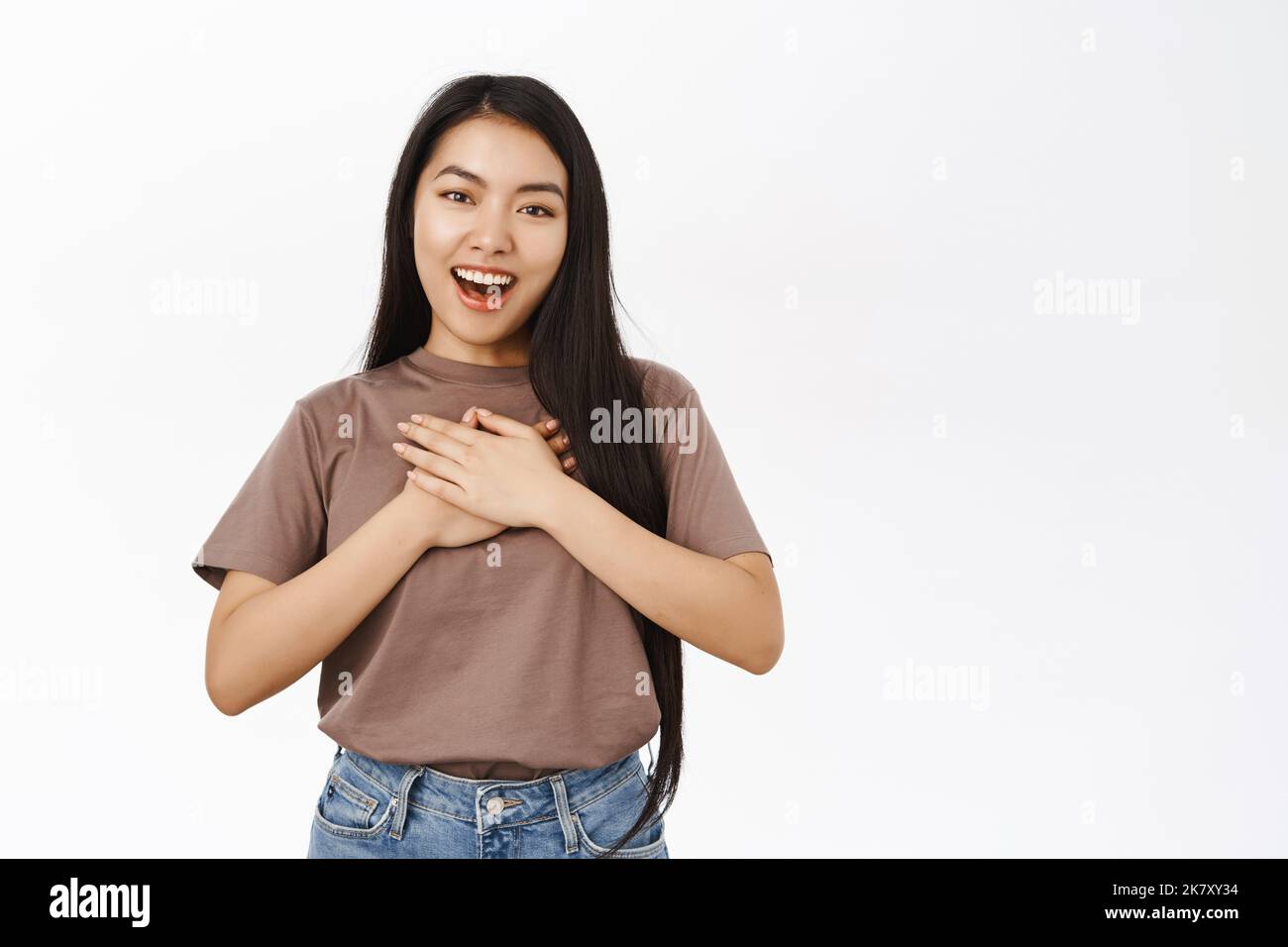 Beautiful korean girl looking with flattered, delighted face, pleased by smth, gazing at smth ...