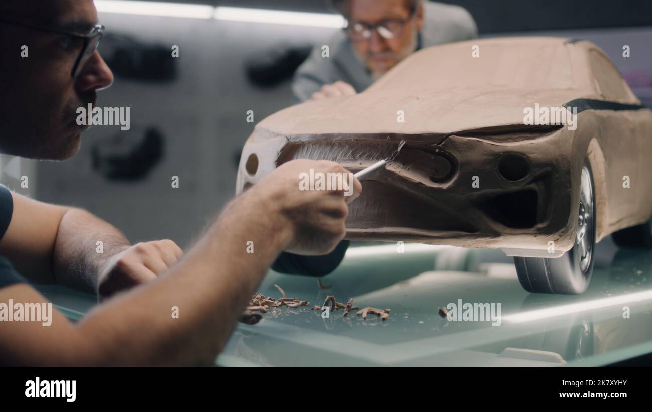 Two male automotive designer sculpting futuristic plasticine clay model ...
