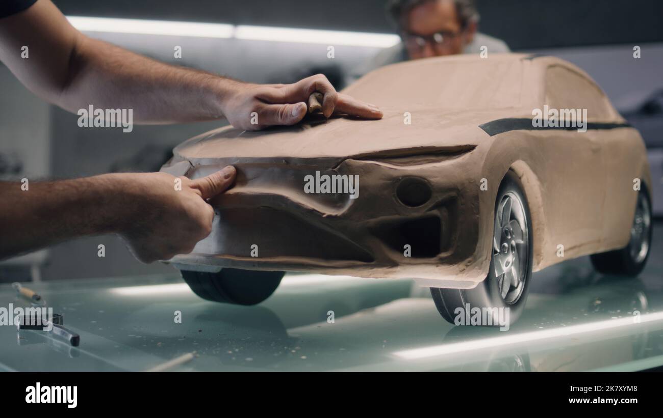 Two male automotive designers creating futuristic plasticine clay model ...