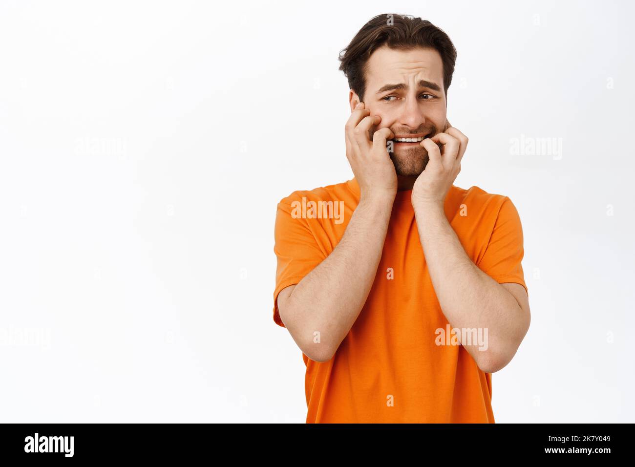 Scared adult man biting his fingernails, looking anxious, standing over ...