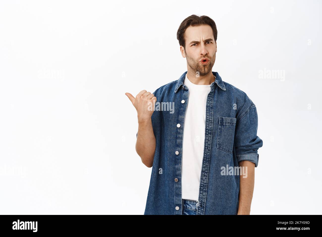 Portrait of impressed guy pointing finger left, showing smth shocking ...