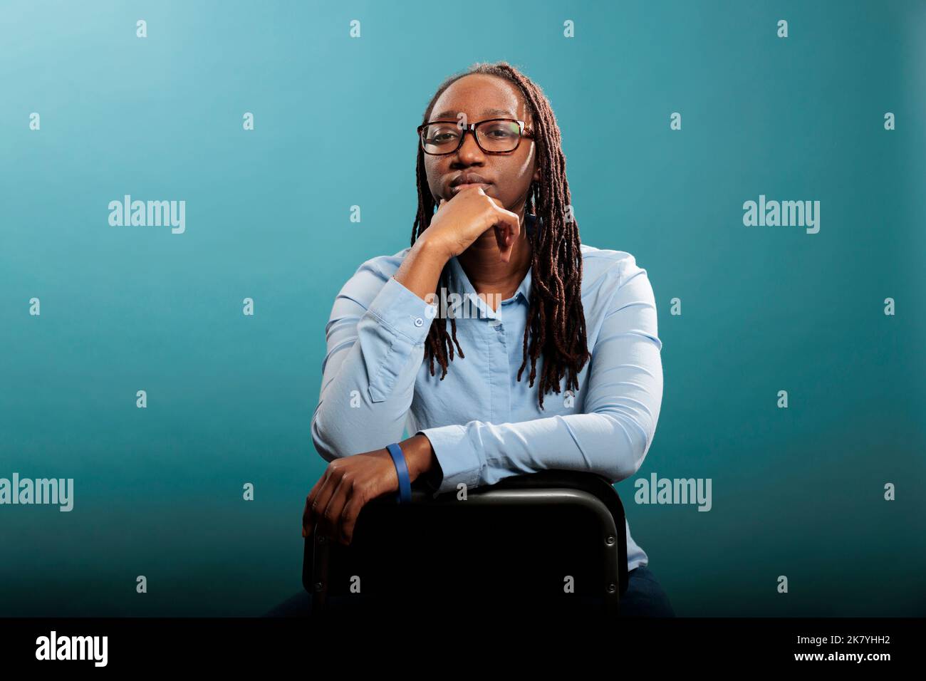 Serious confident woman sitting on chair while looking at camera on ...
