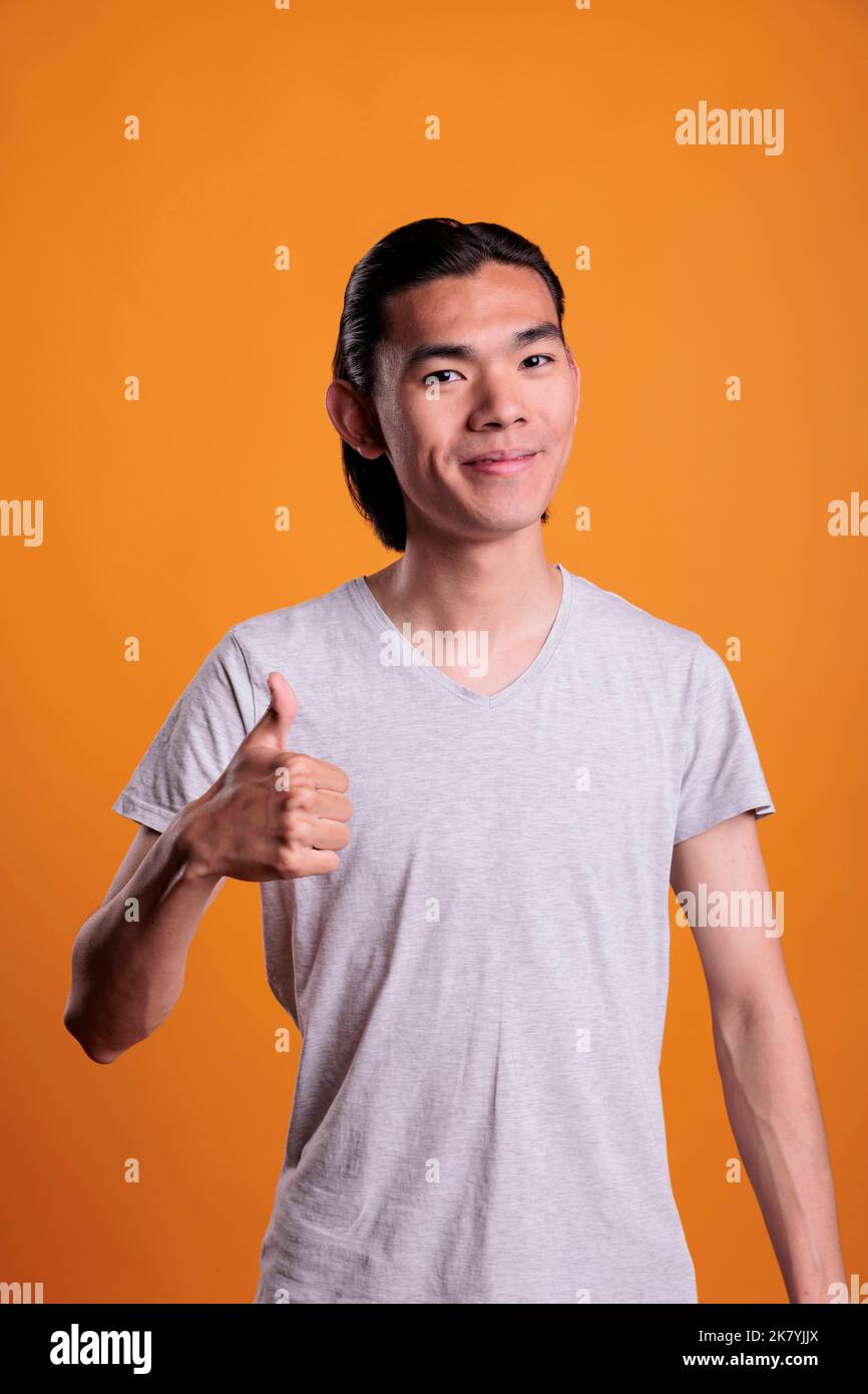 Young cheerful smiling asian man giving thumb up, medium shot portrait ...