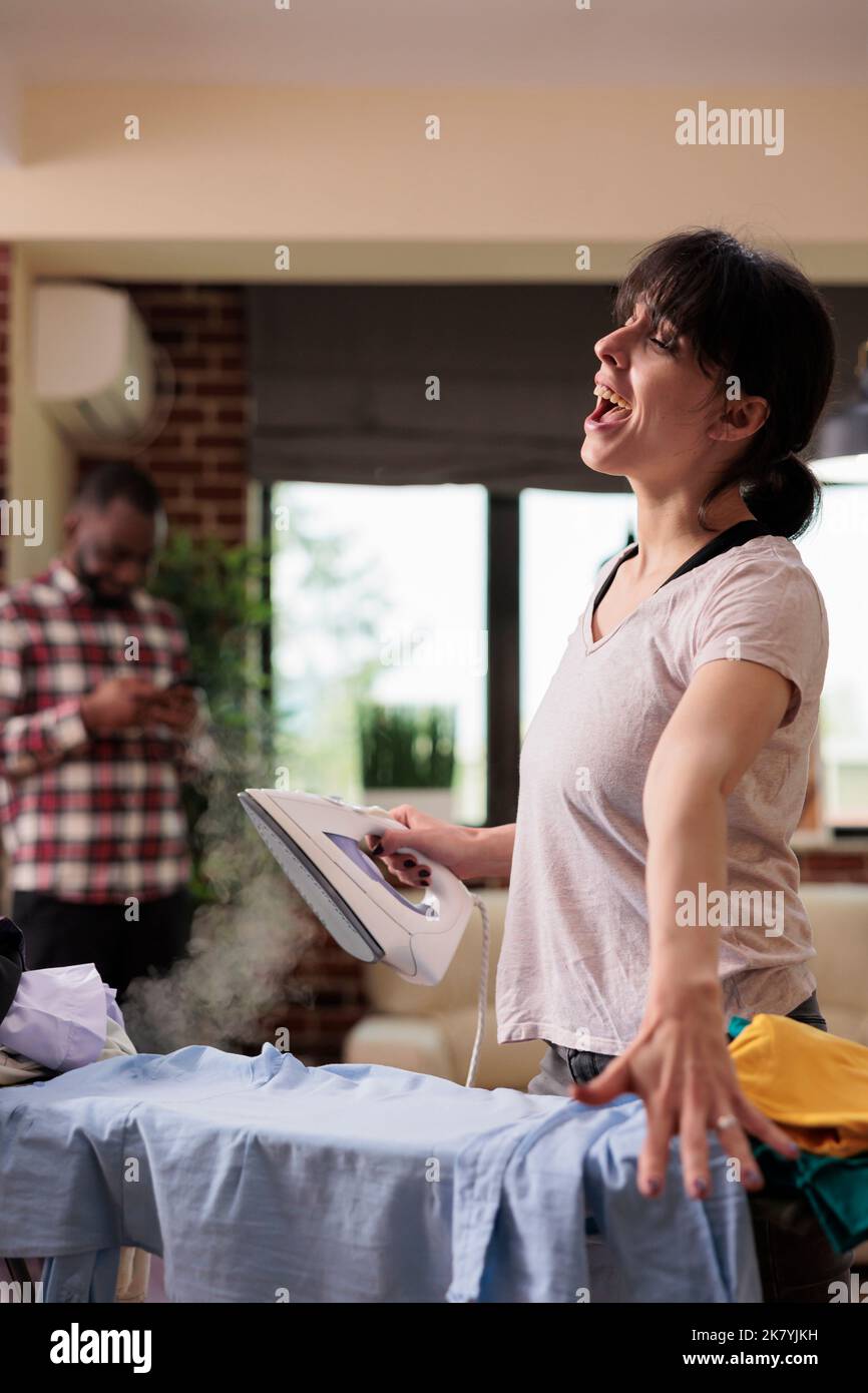 Cheerful housewife enjoying while doing household chores singing ...