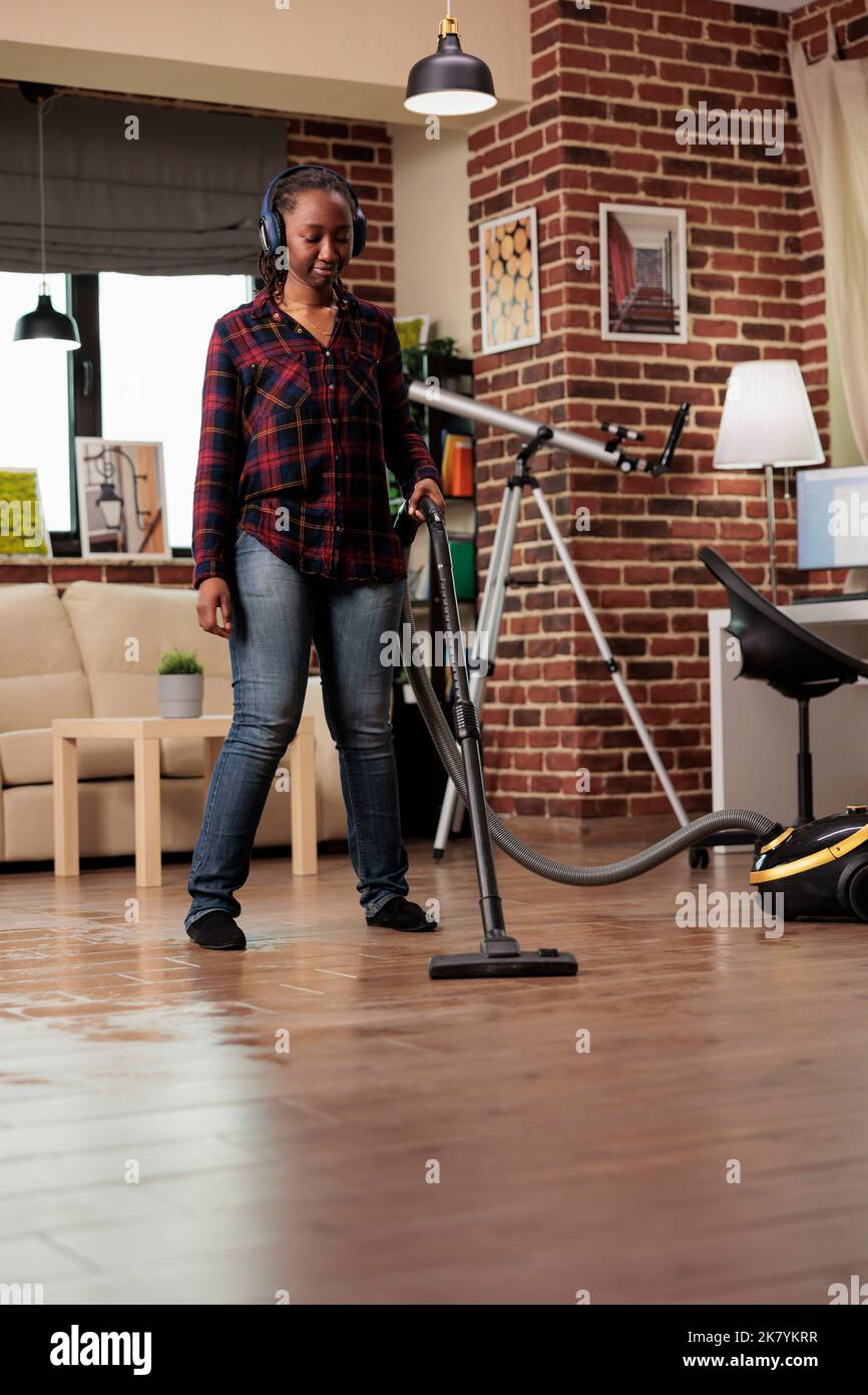 Housewife using modern vacuum cleaner listening to favorite music with ...