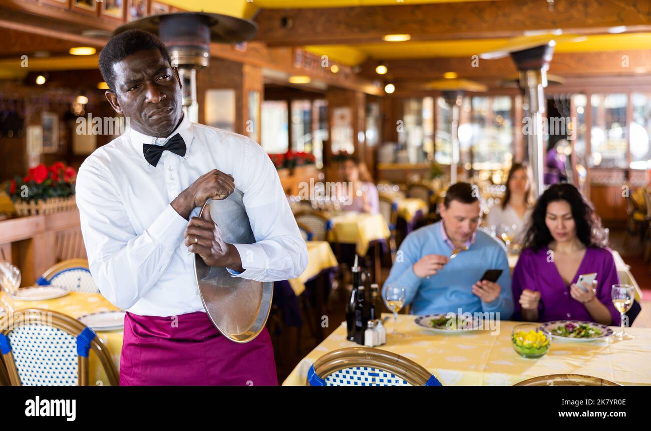 Tired african american waiter with empty serving tray in restaurant ...