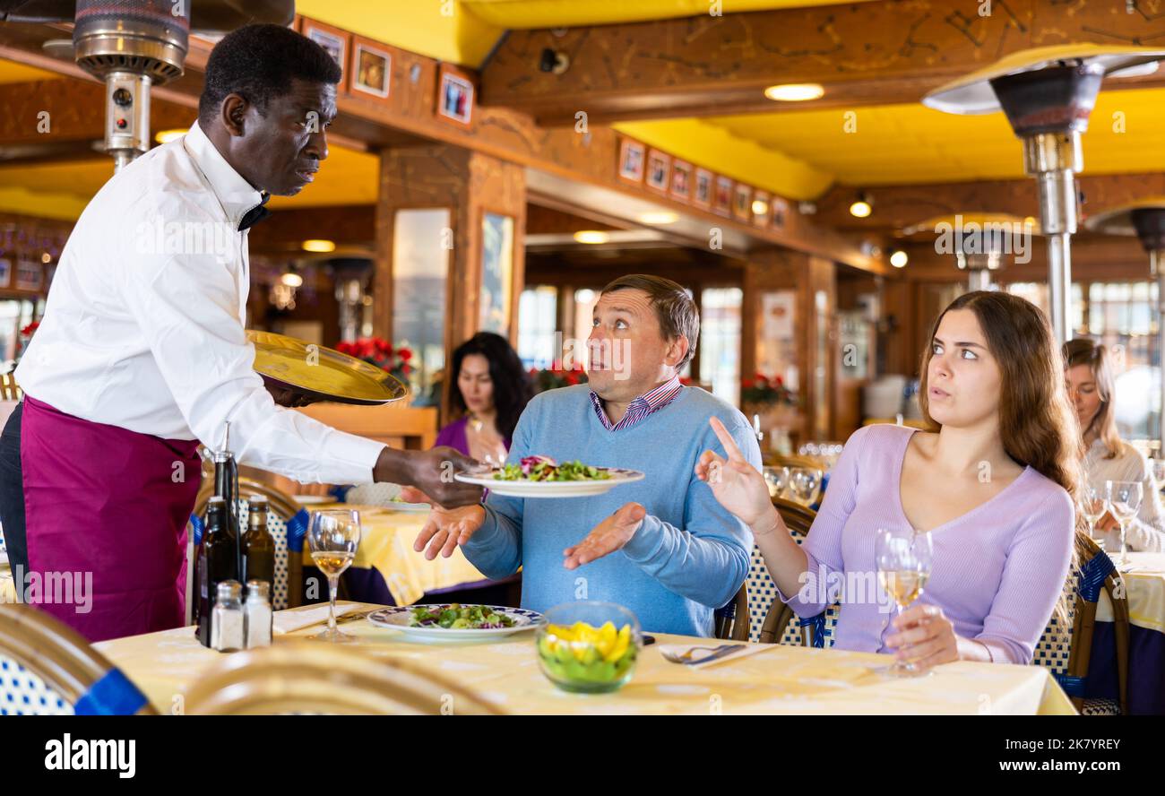 Displeased angry couple sitting at table in restaurant, talking with ...