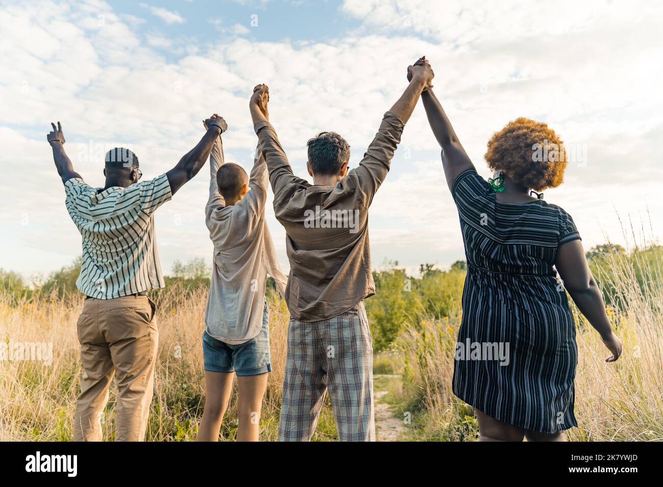 Multinational group of four people standing together holding hands in ...