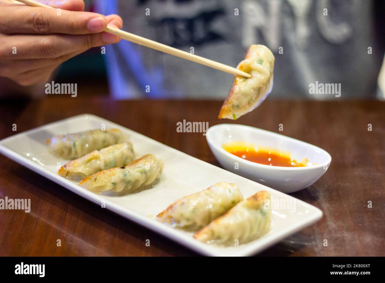 A diner about to dip an asian pot sticker dumpling into a hot sauce at ...