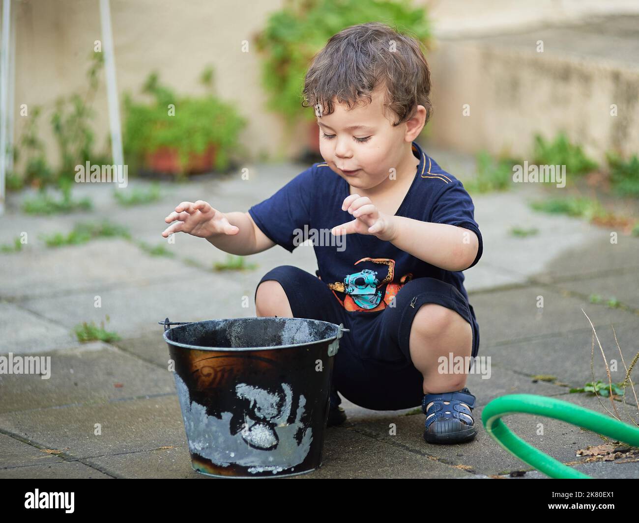 young boy playing with a watering hose and buckets in the backyard ...