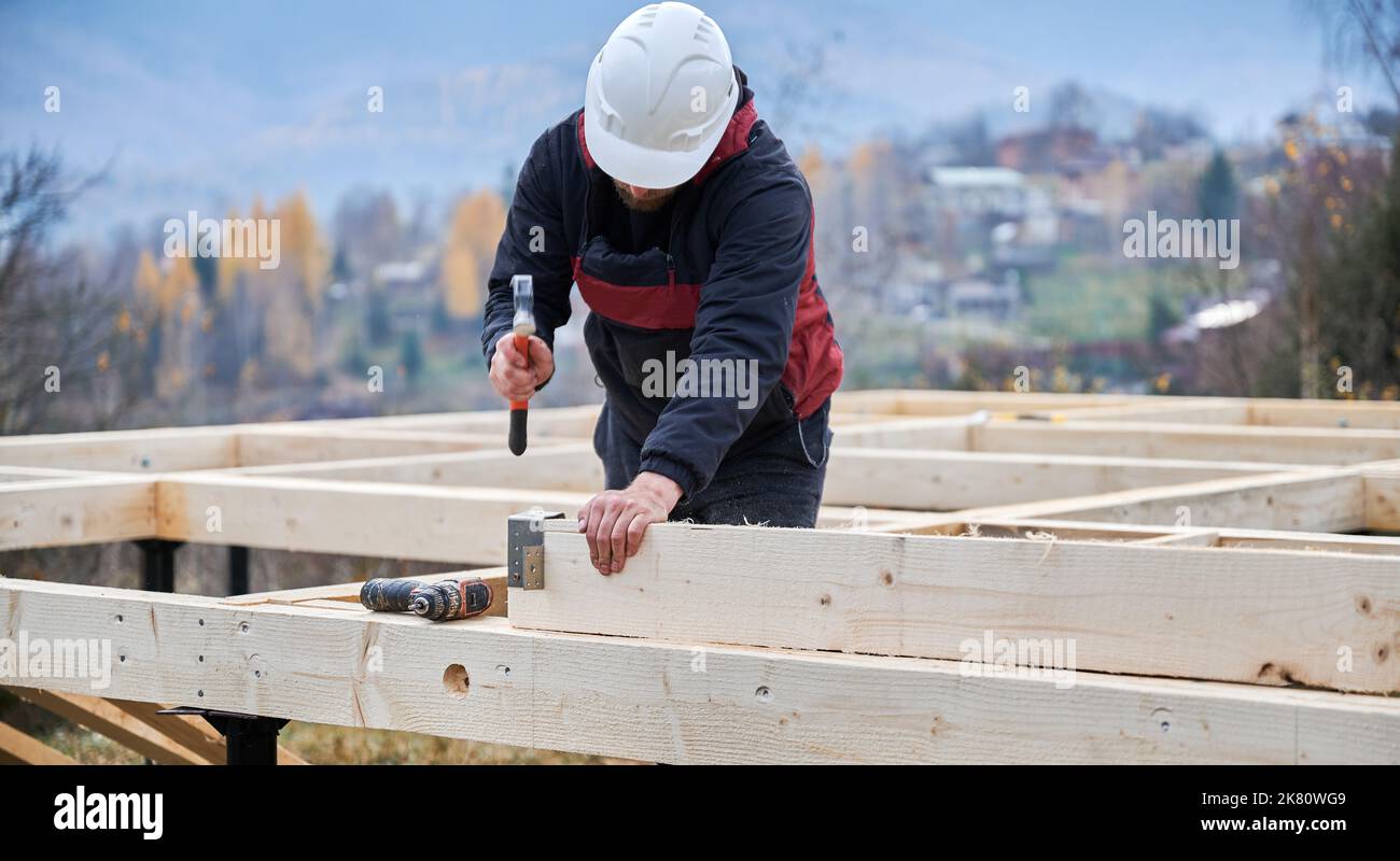 Man worker building wooden frame house on pile foundation. Carpenter ...