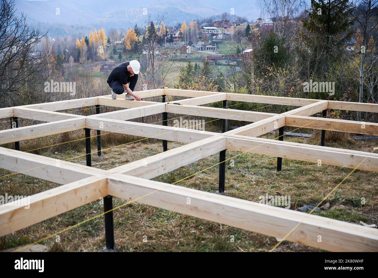 Man worker building wooden frame house on pile foundation. Carpenter ...