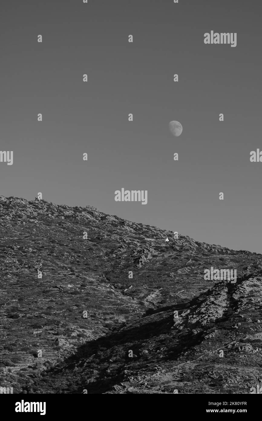 View of a mountain with a single white chapel and the moon in the blue ...