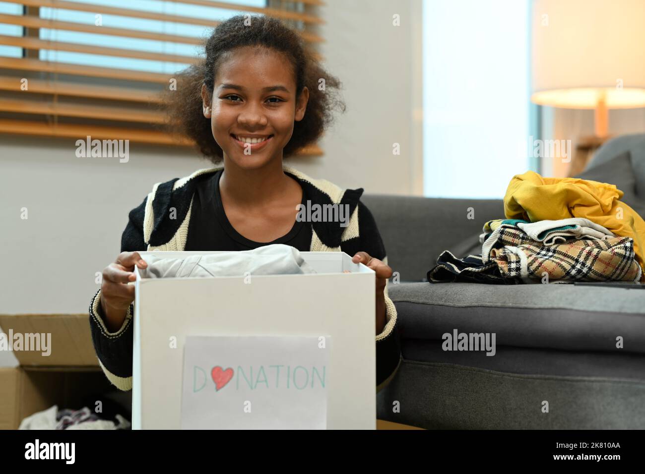 Happy young woman holding box of clothes with donate label and smiling ...