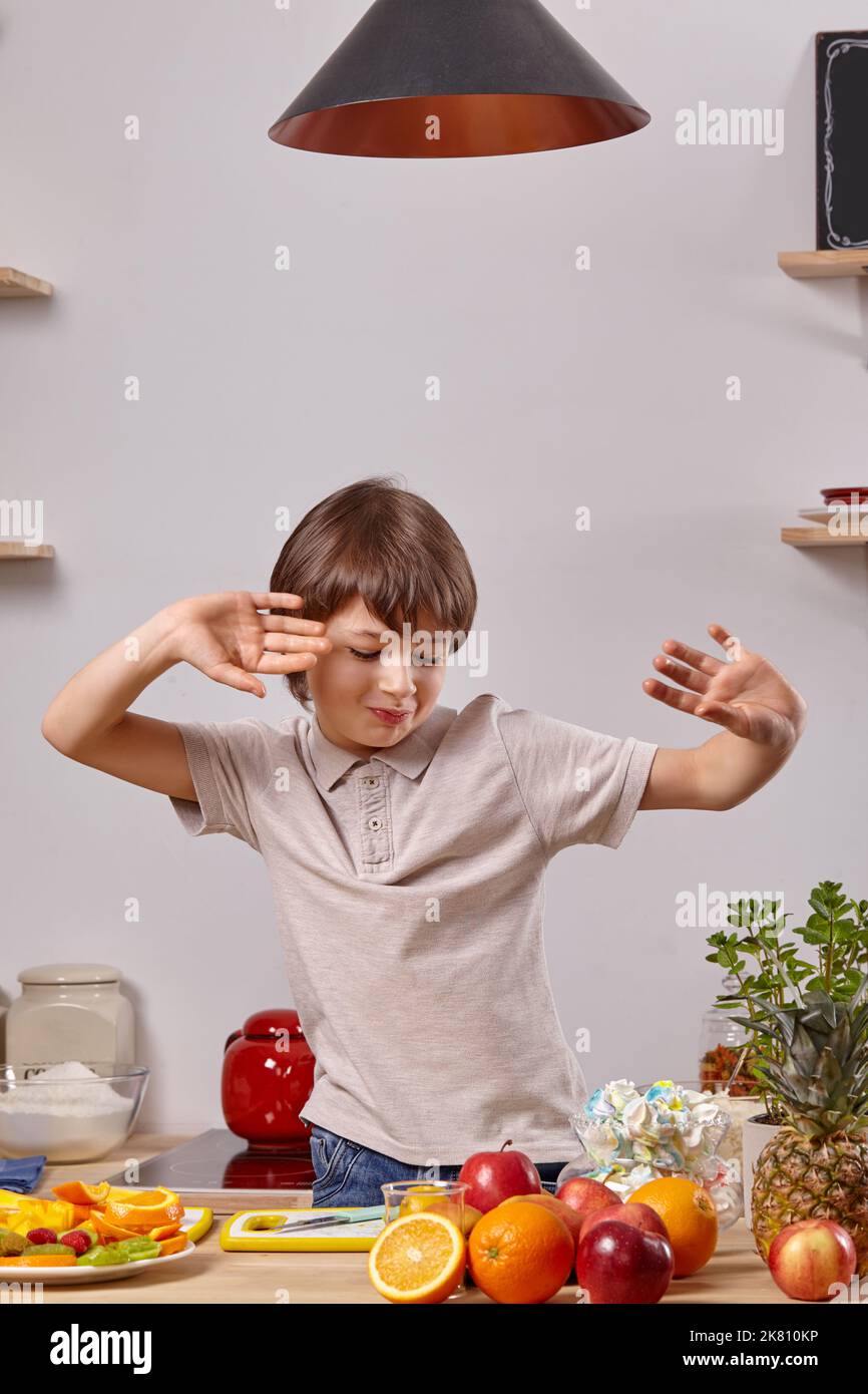 Cute little boy with brown hair is cooking at a kitchen against a white ...